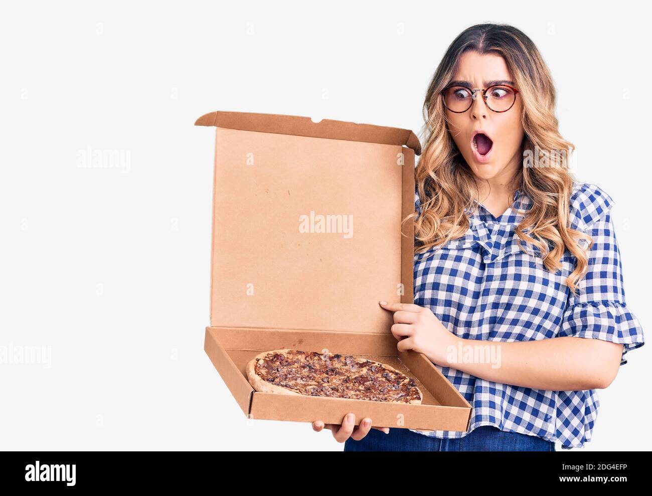 Young caucasian woman holding delivery pizza box scared and amazed with ...