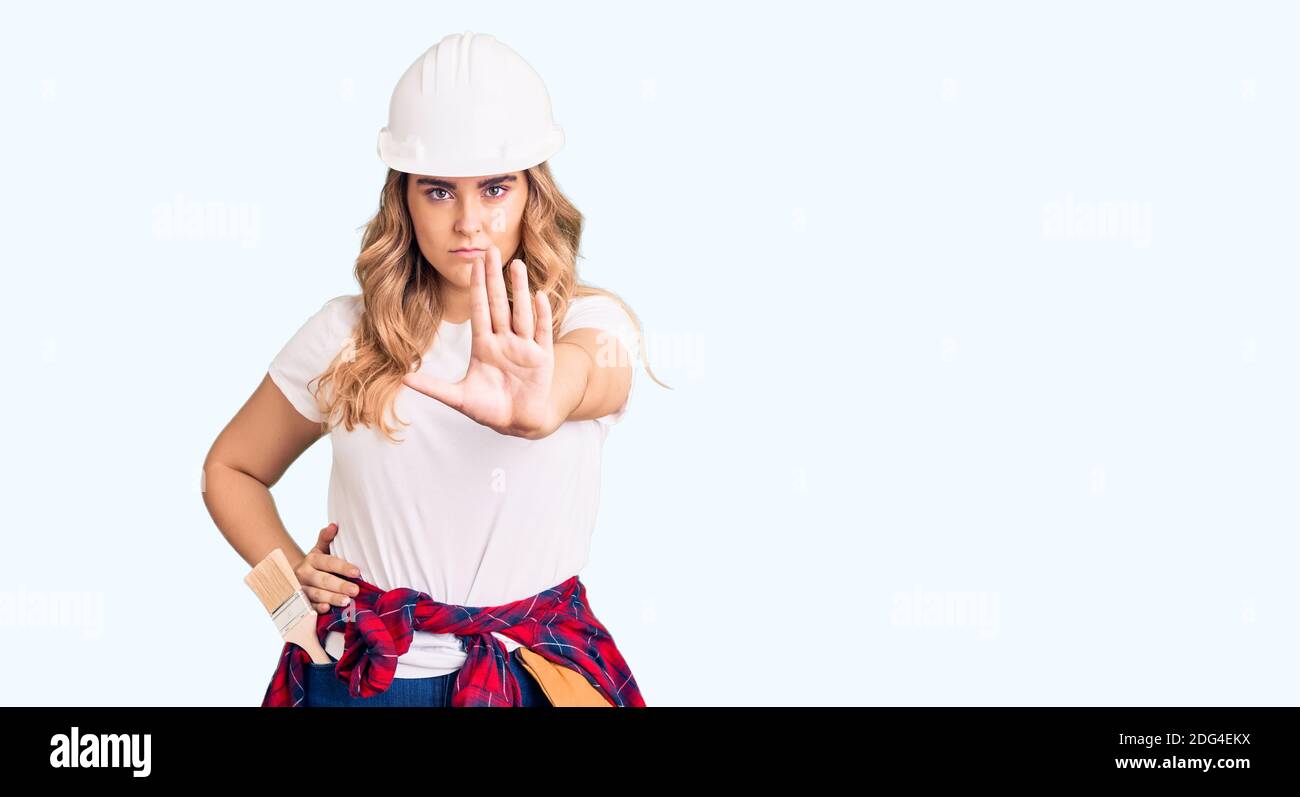 Young caucasian woman wearing security helmet doing stop sing with palm ...