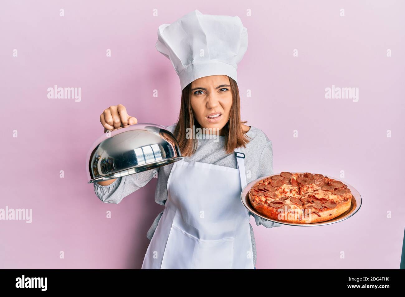 Young beautiful woman professional cook holding italian pizza clueless ...