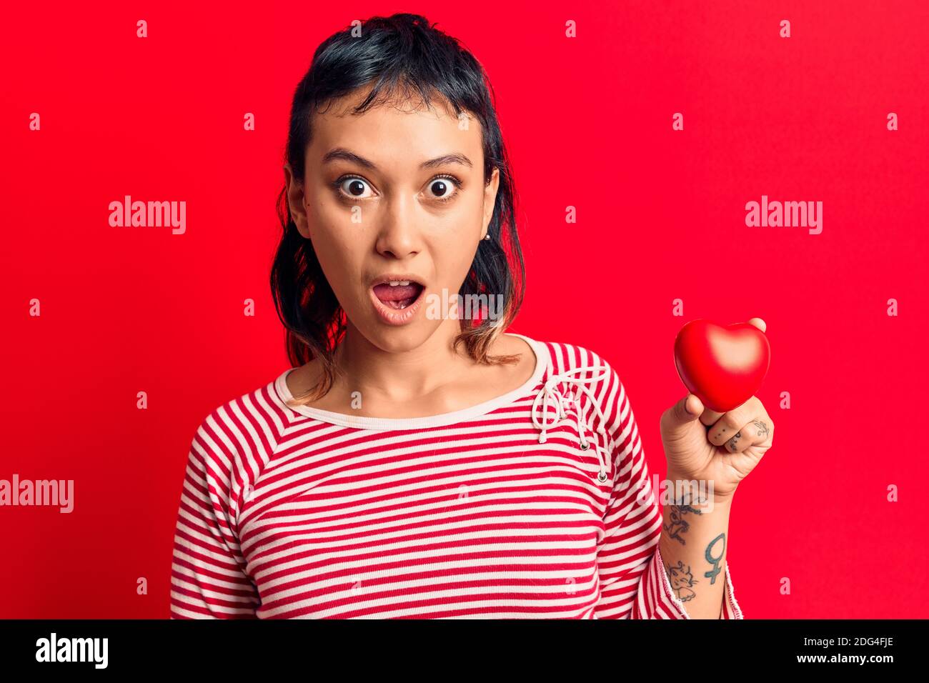 Young woman holding heart scared and amazed with open mouth for ...