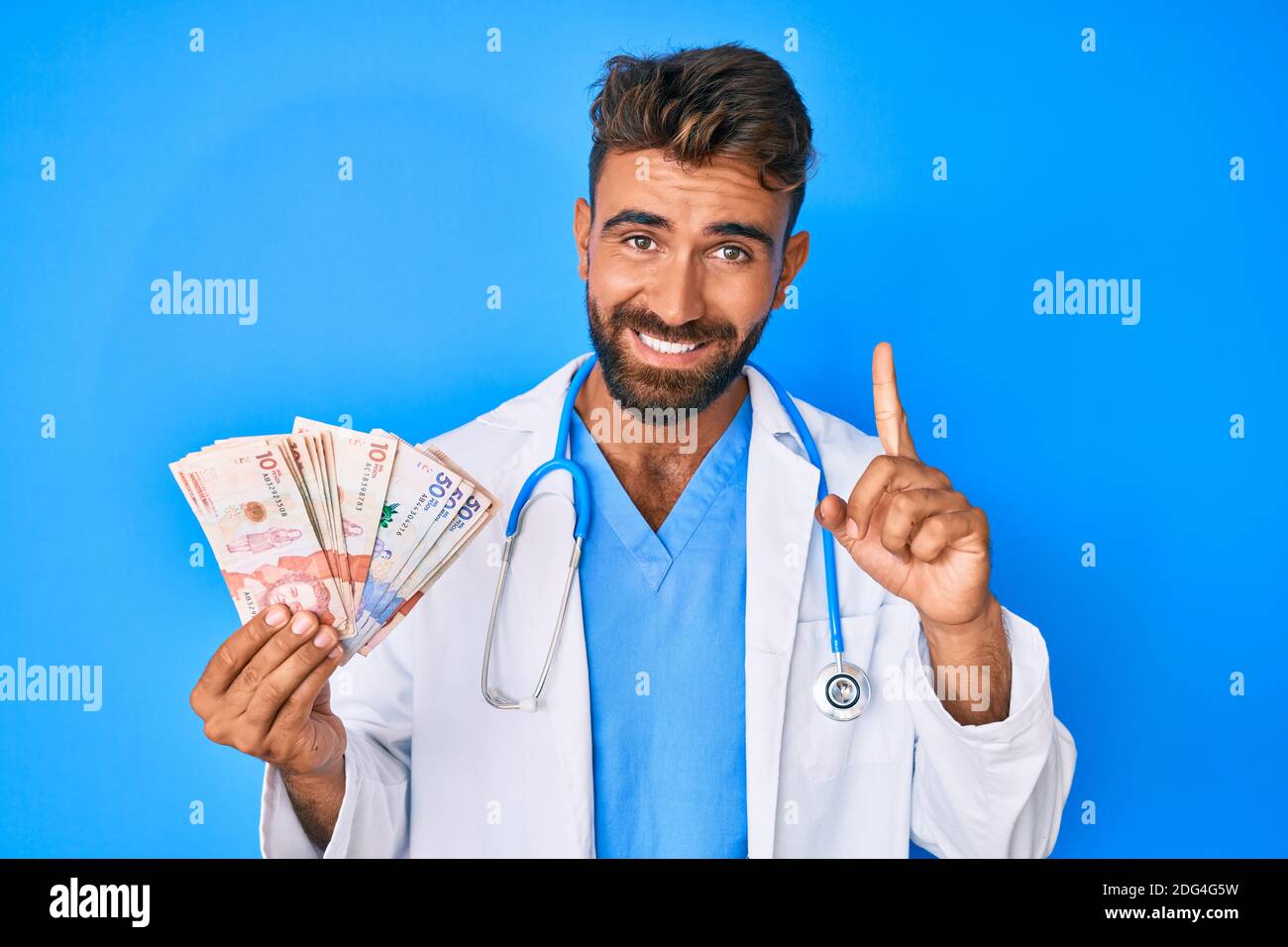Young hispanic man wearing doctor uniform holding colombian pesos ...