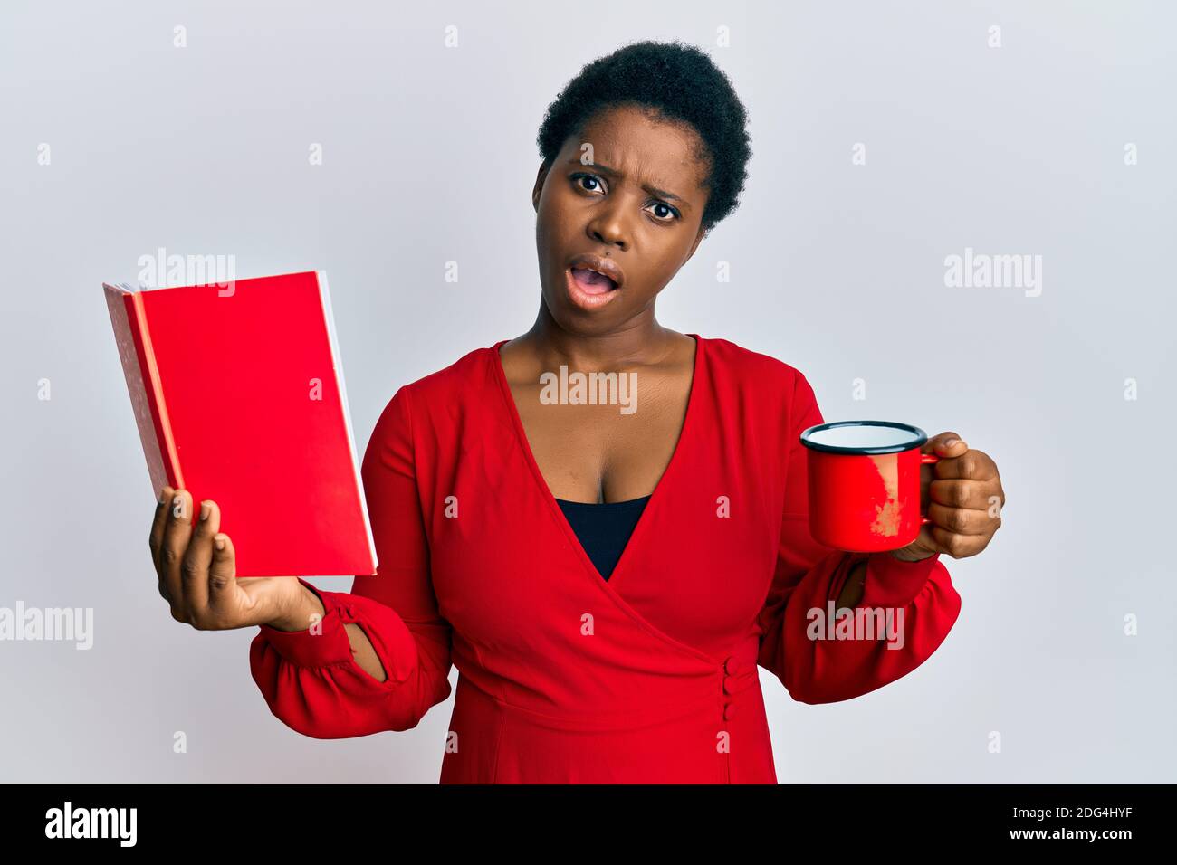 Young african woman with short hair reading a book and drinking a cup ...
