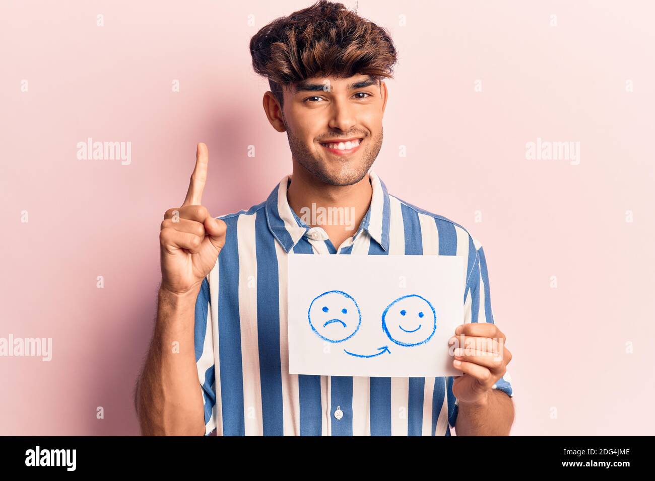 Young hispanic man holding sad to happy emotion paper smiling with an ...
