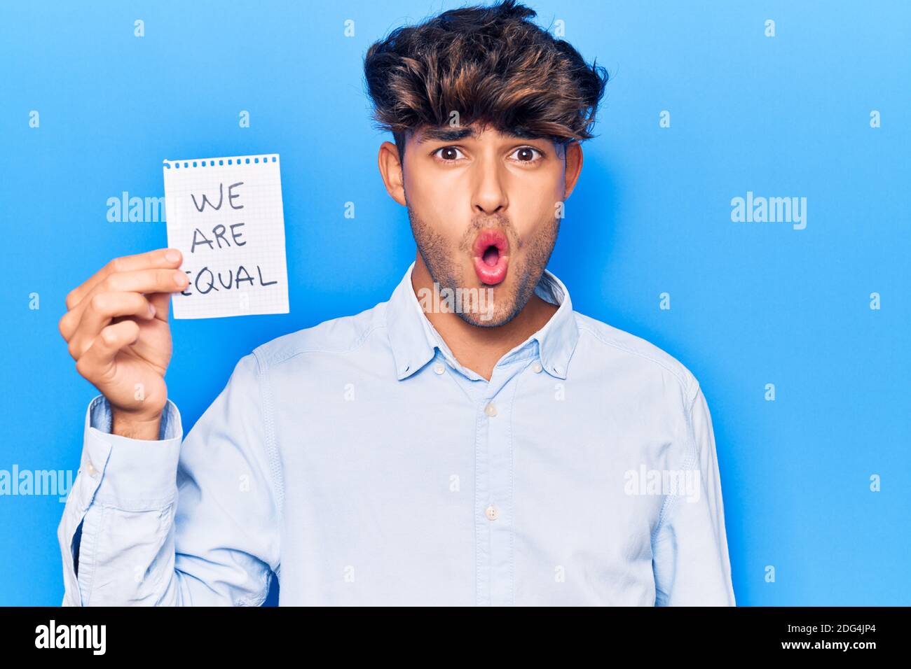 Young hispanic man holding we are equal paper scared and amazed with ...