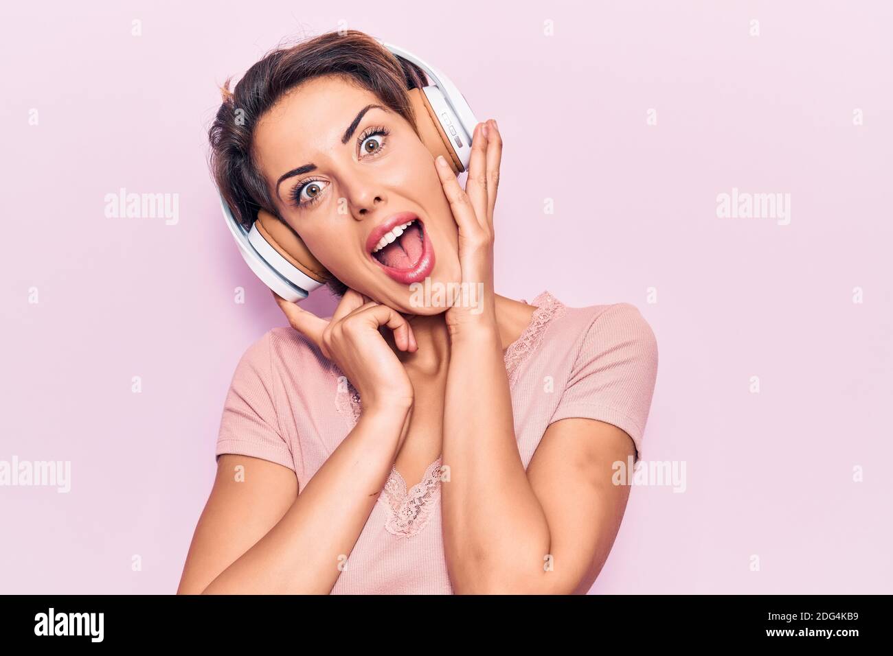 Young beautiful woman listening to music using headphones scared and ...