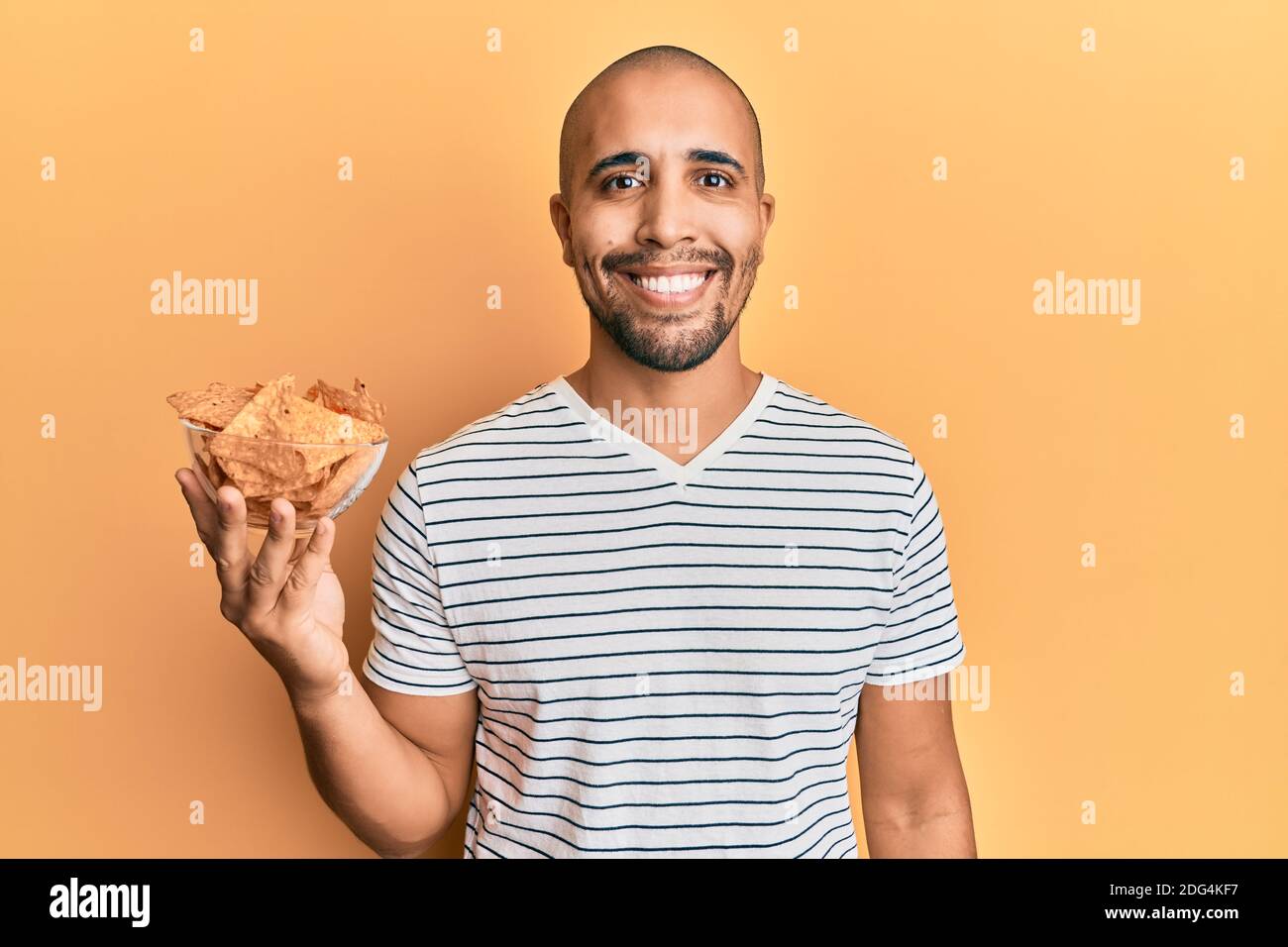 Hispanic adult man holding nachos potato chips looking positive and ...