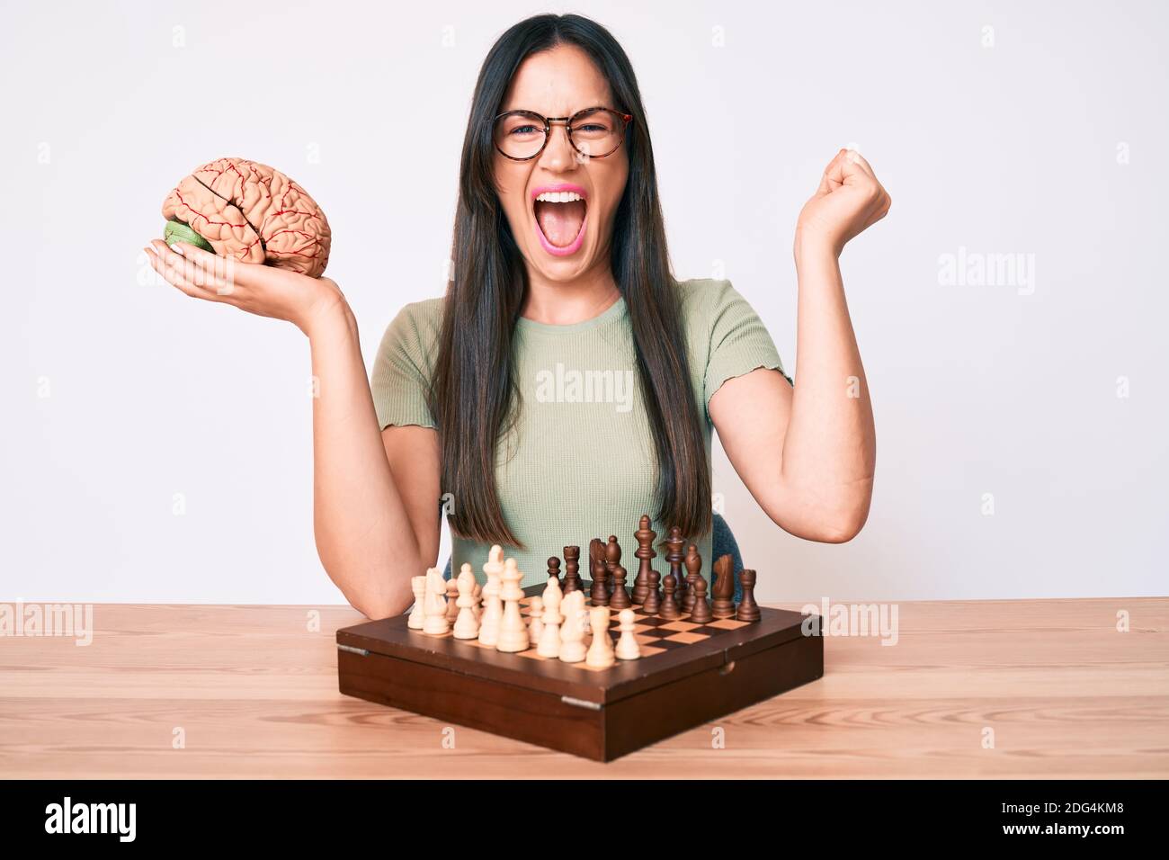 Young caucasian woman sitting at the desk playing chess holding brain ...