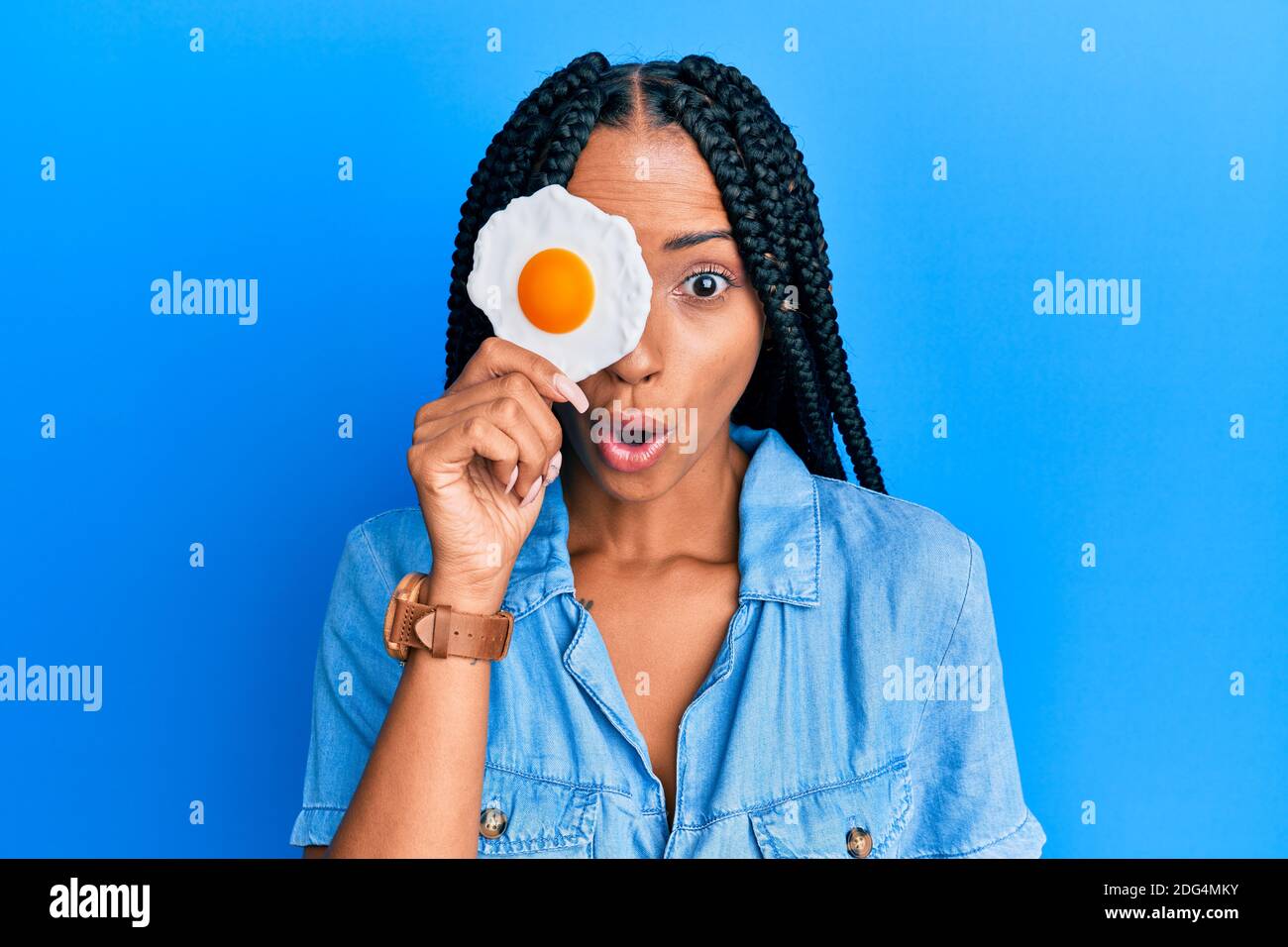 Beautiful hispanic woman holding fried egg scared and amazed with open ...