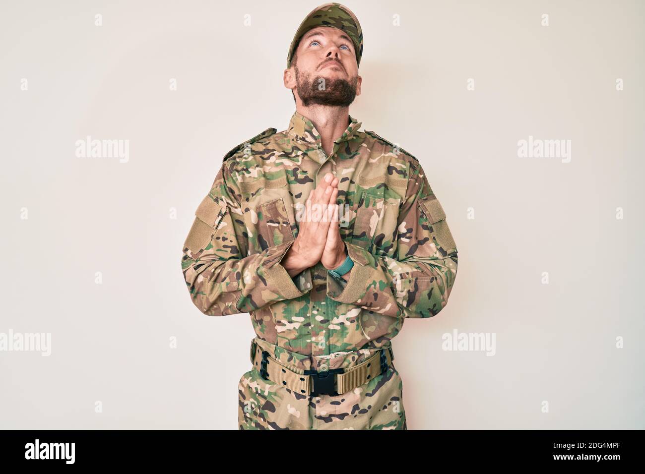 Young caucasian man wearing camouflage army uniform begging and praying ...