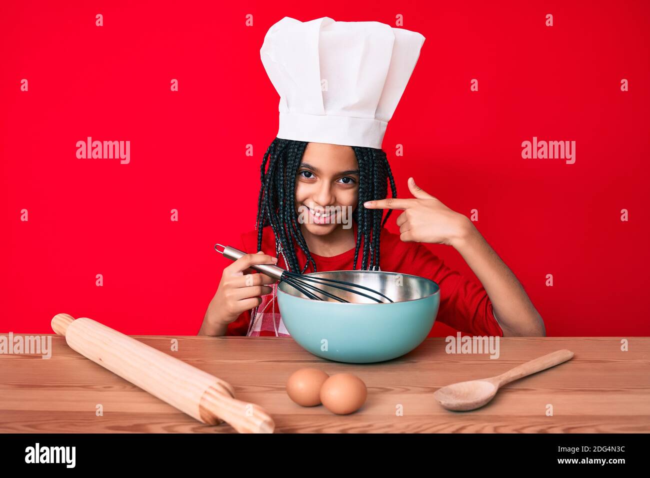 Young african american girl child with braids cooking using baker whisk ...