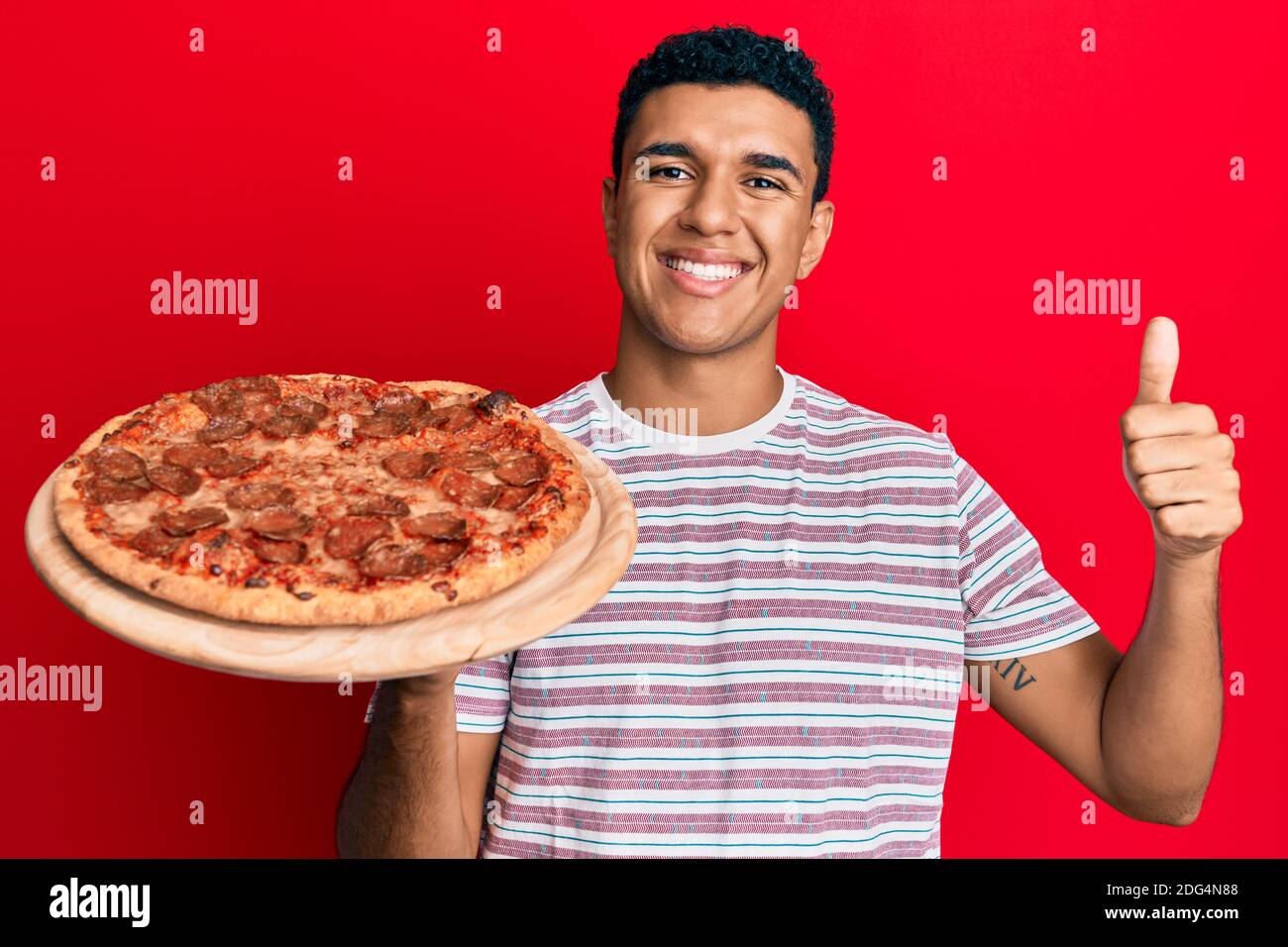 Young arab man holding italian pizza smiling happy and positive, thumb ...