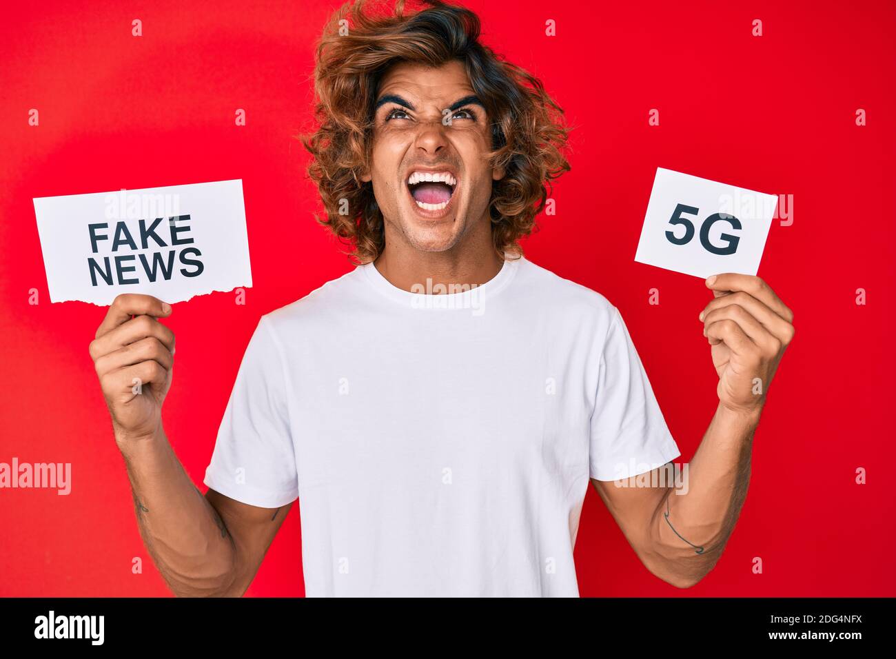 Young hispanic man holding fake news and 5g banner angry and mad ...