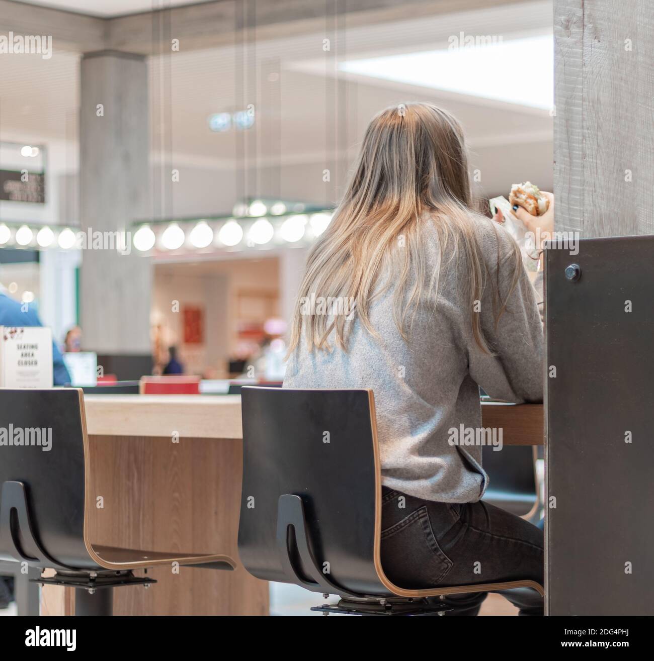 Back view of young girl sitting in indoors food court and eating an ...