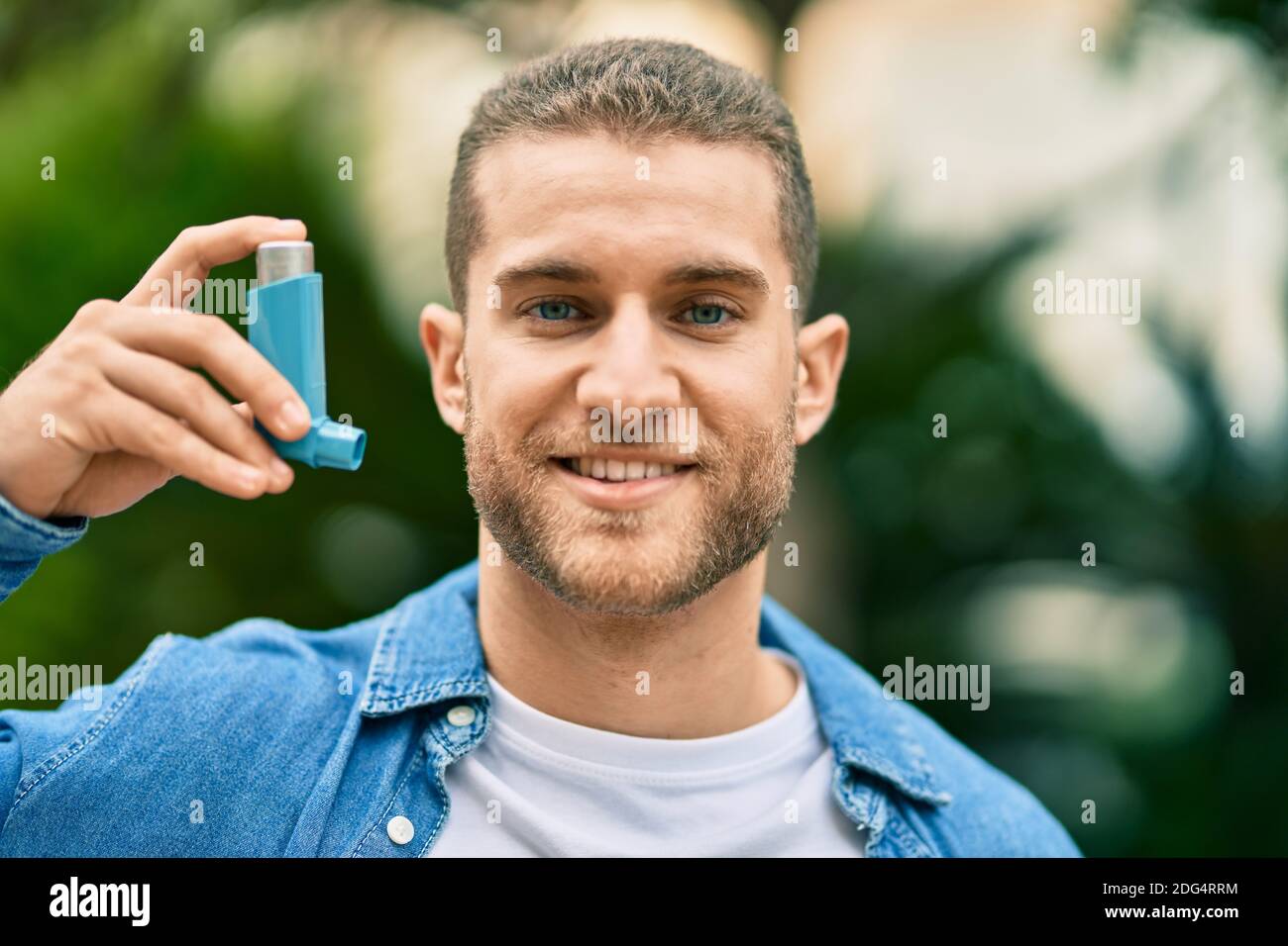 Young caucasian asthmatic man smiling happy holding inhaler at the park ...