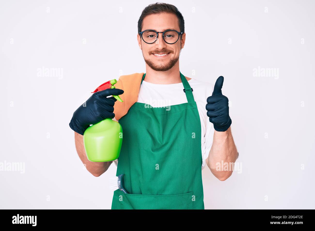 Young handsome man wearing apron holding sprayer smiling happy and ...