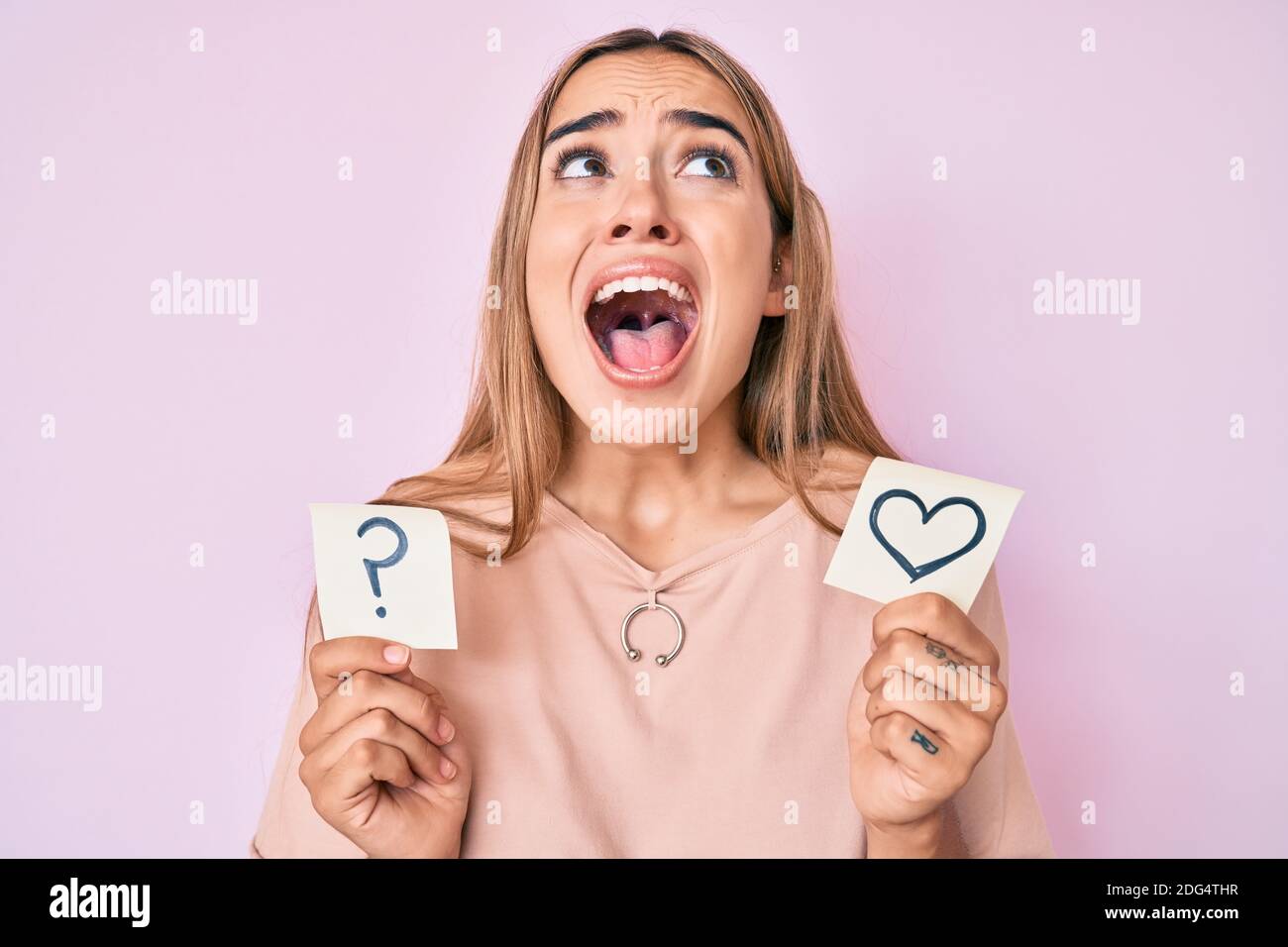 Young beautiful blonde woman holding heart and question mark reminder ...