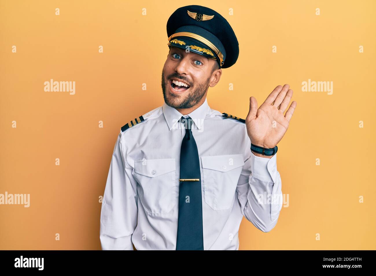 Handsome hispanic man wearing airplane pilot uniform waiving saying ...