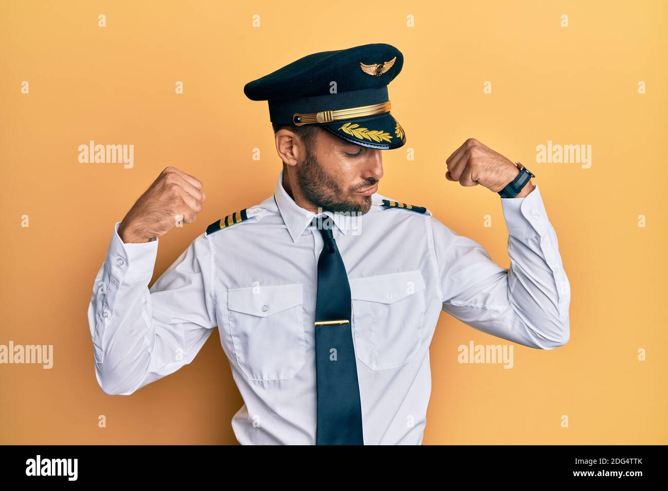 Handsome hispanic man wearing airplane pilot uniform showing arms ...