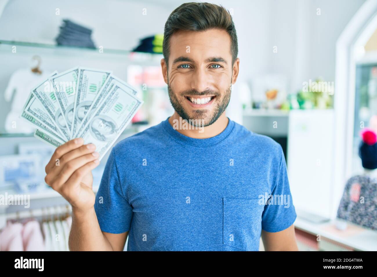 Young handsome man smiling happy holding dollars at clothing store ...