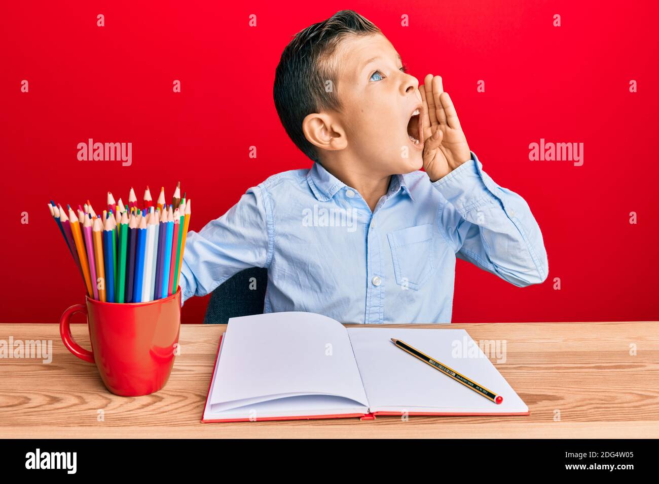 Adorable caucasian kid writing book sitting on the table shouting and ...