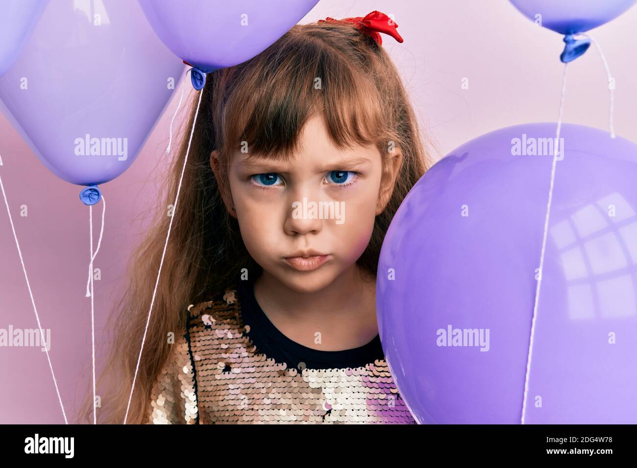 Little caucasian girl kid holding balloons skeptic and nervous ...