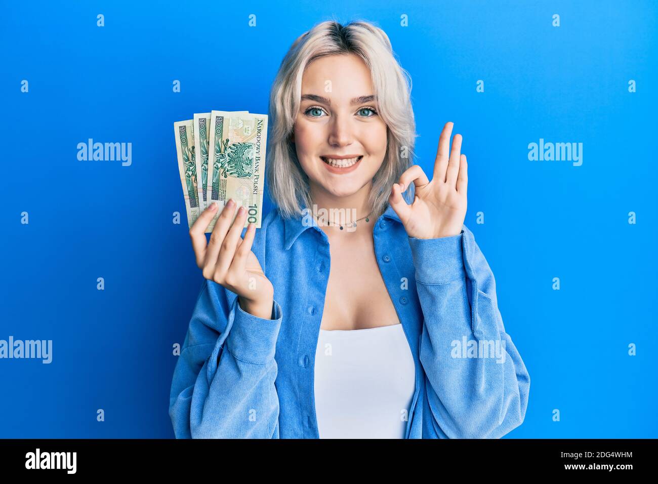 Young blonde girl holding 50 polish zloty banknotes doing ok sign with ...
