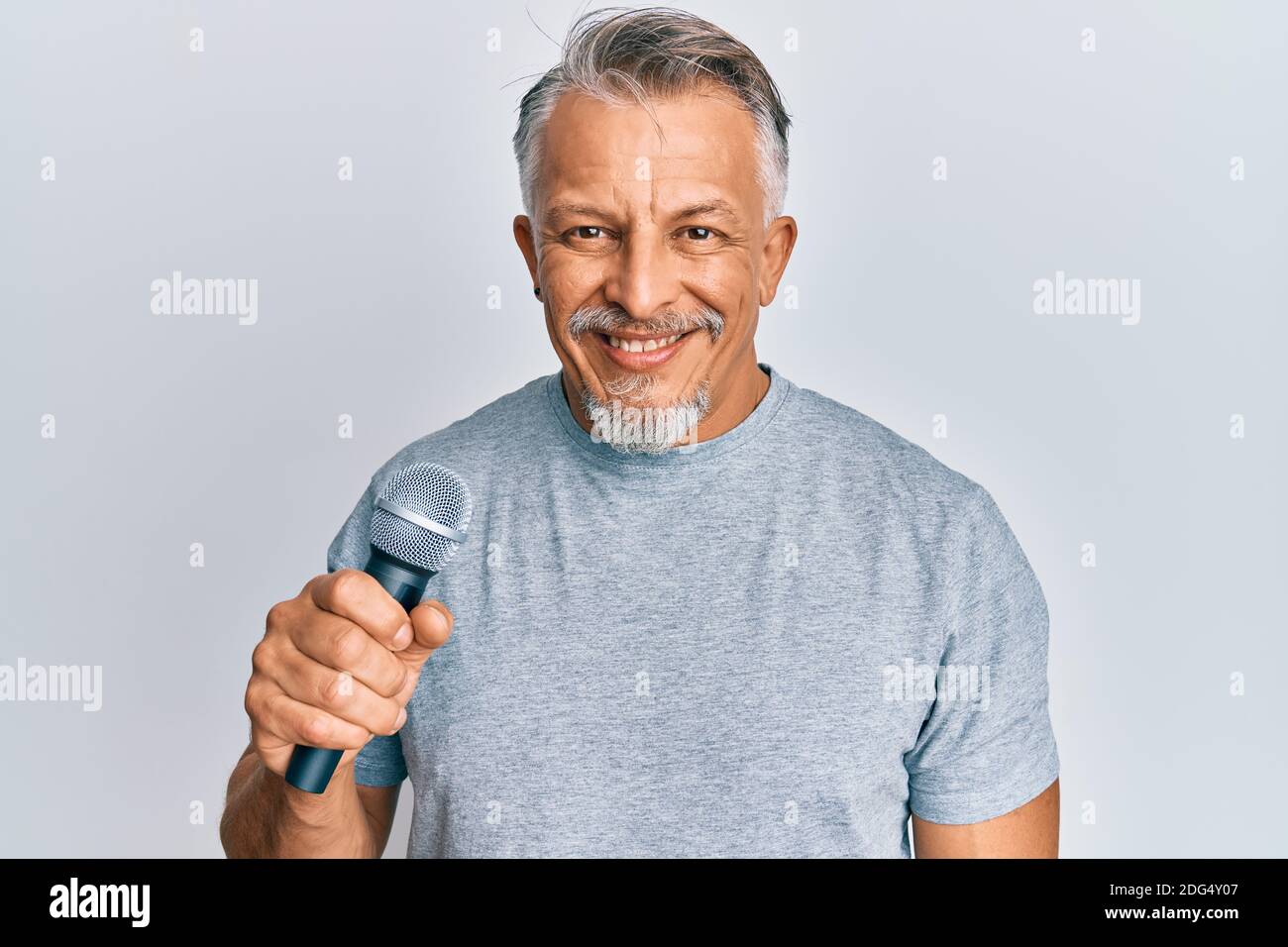 Middle age grey-haired man singing song using microphone looking ...