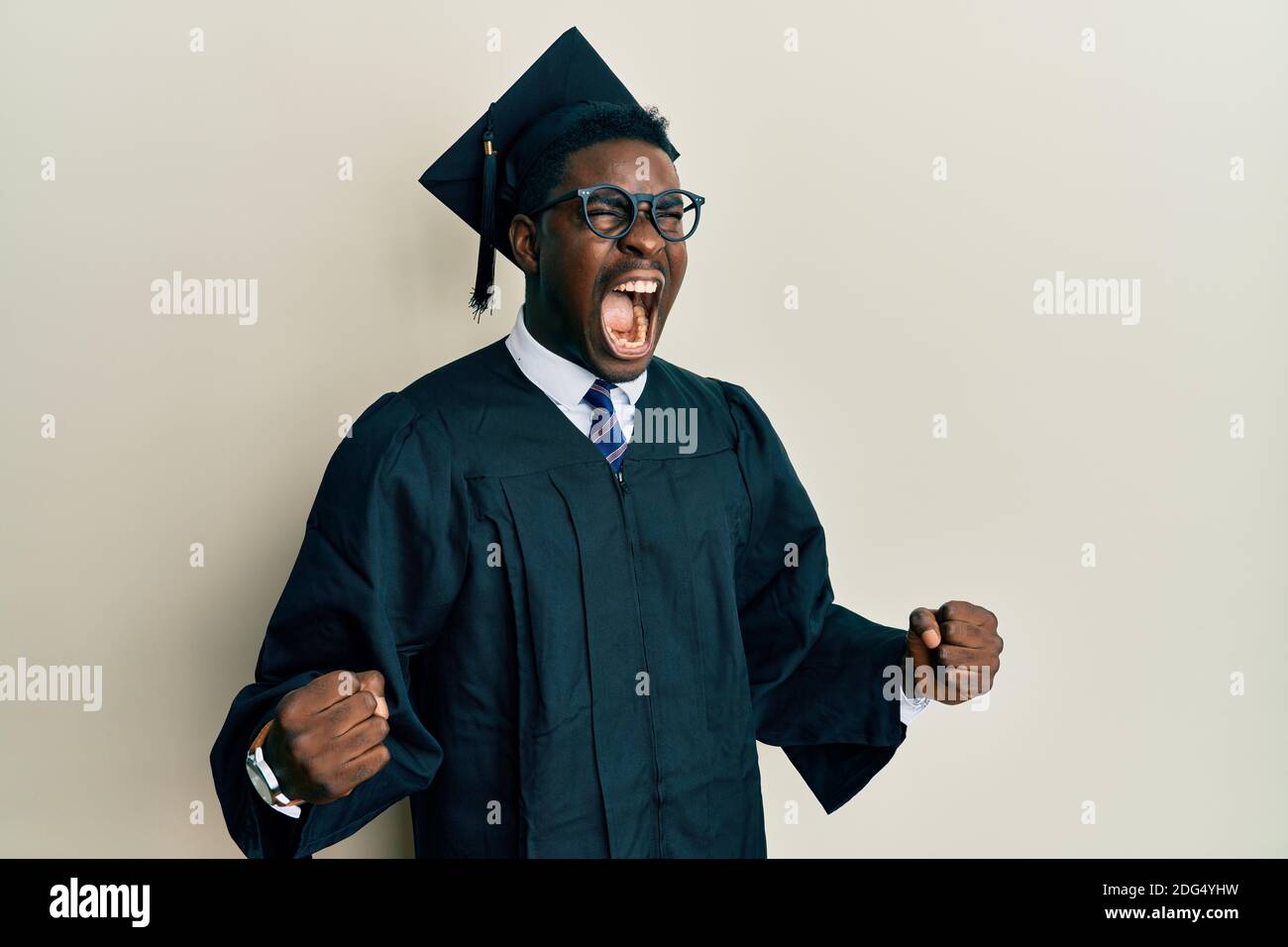 Handsome black man wearing graduation cap and ceremony robe angry and ...