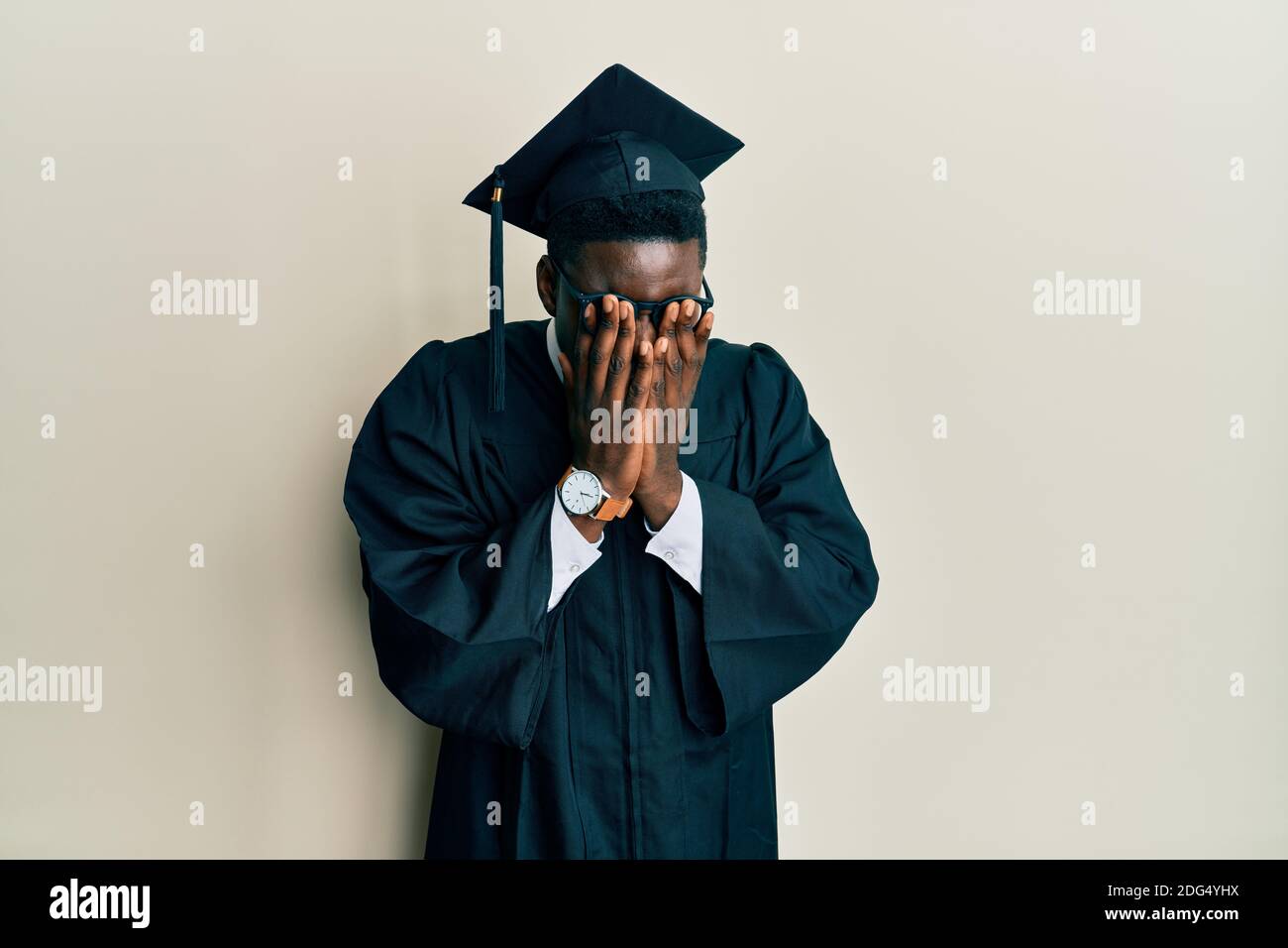 Handsome black man wearing graduation cap and ceremony robe rubbing ...