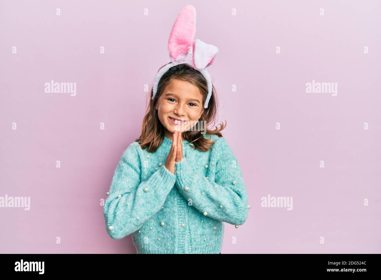 Little beautiful girl wearing cute easter bunny ears praying with hands ...