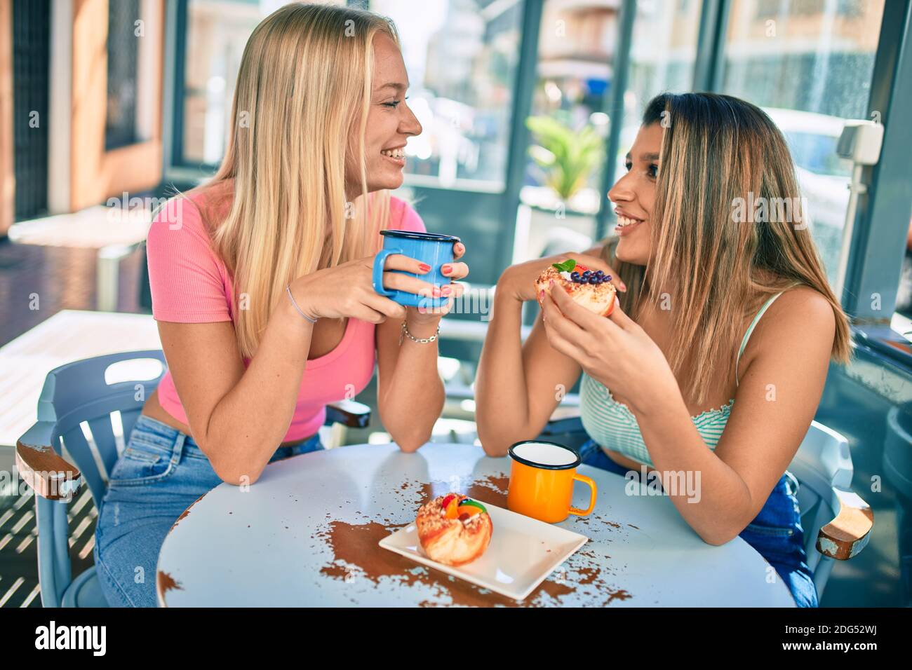 Two beautiful and young girl friends together having fun at cafeteria ...