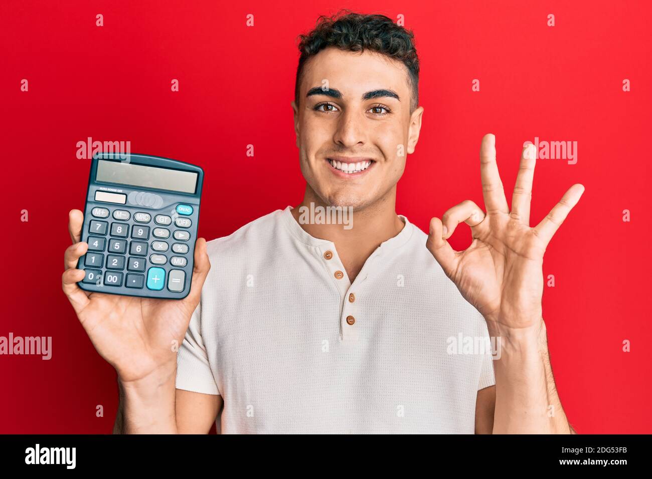 Hispanic young man showing calculator device doing ok sign with fingers ...
