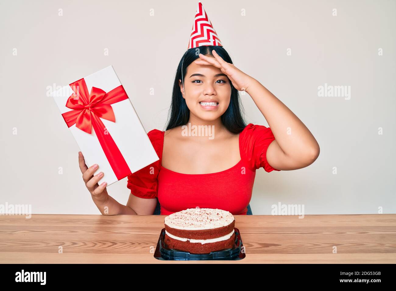 Young asian girl wearing birthday hat holding present stressed and ...
