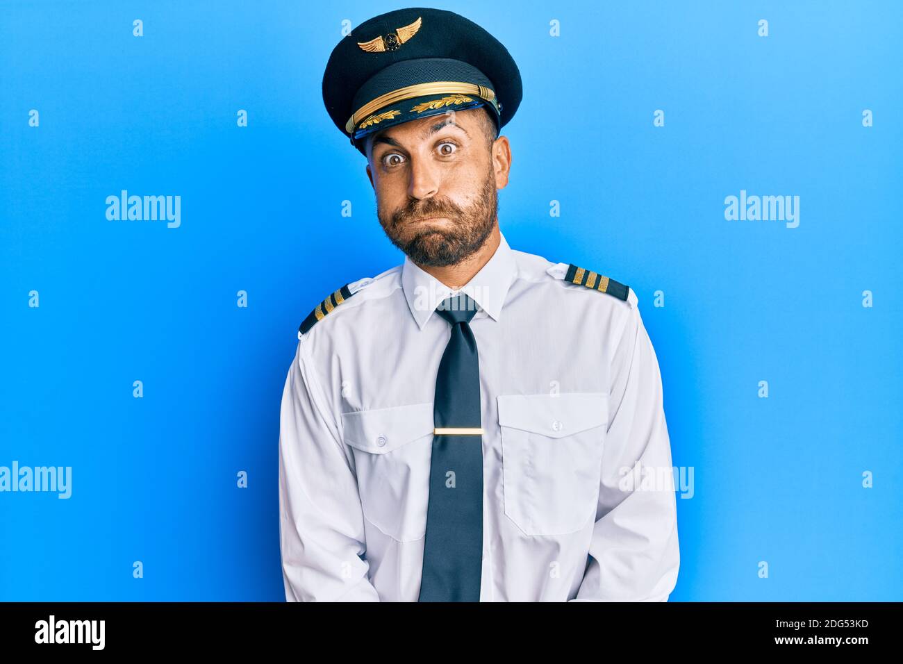 Handsome man with beard wearing airplane pilot uniform puffing cheeks ...