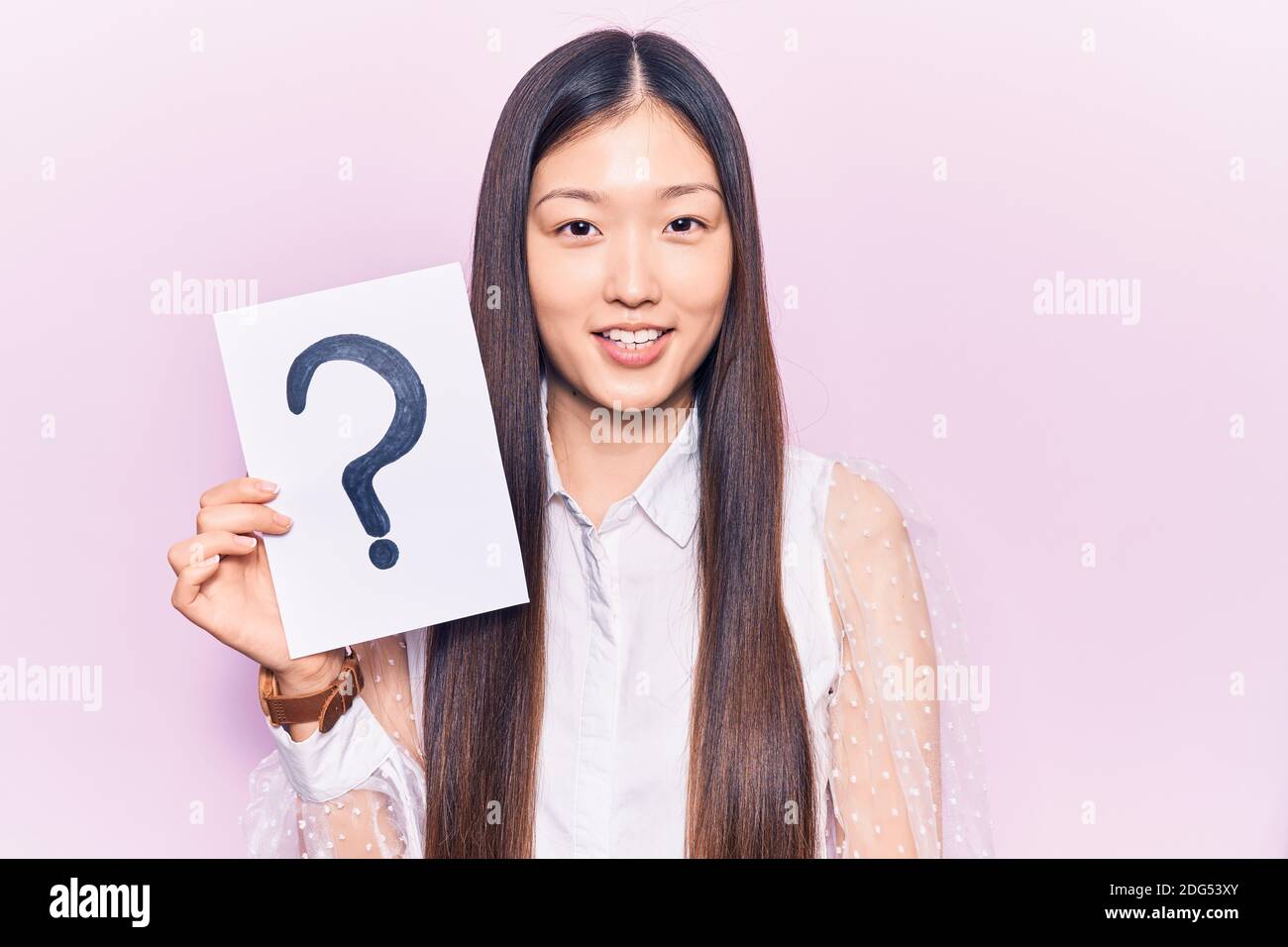 Young beautiful chinese woman holding question mark looking positive ...