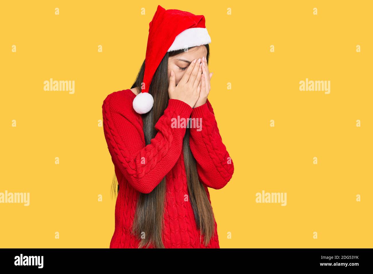 Young chinese woman wearing christmas hat with sad expression covering ...