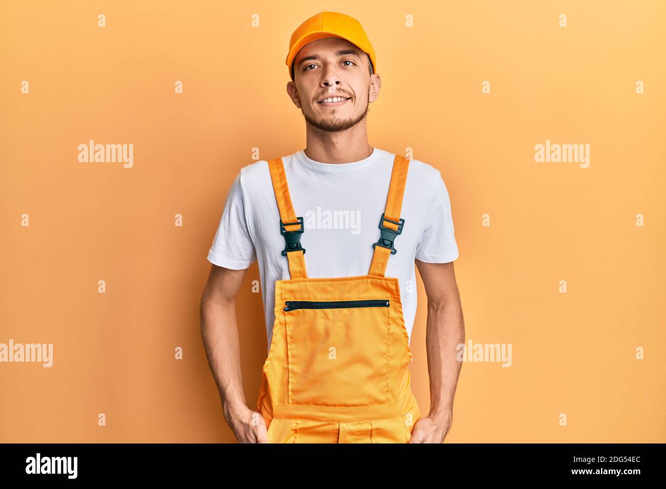 Hispanic young man wearing handyman uniform with a happy and cool smile ...