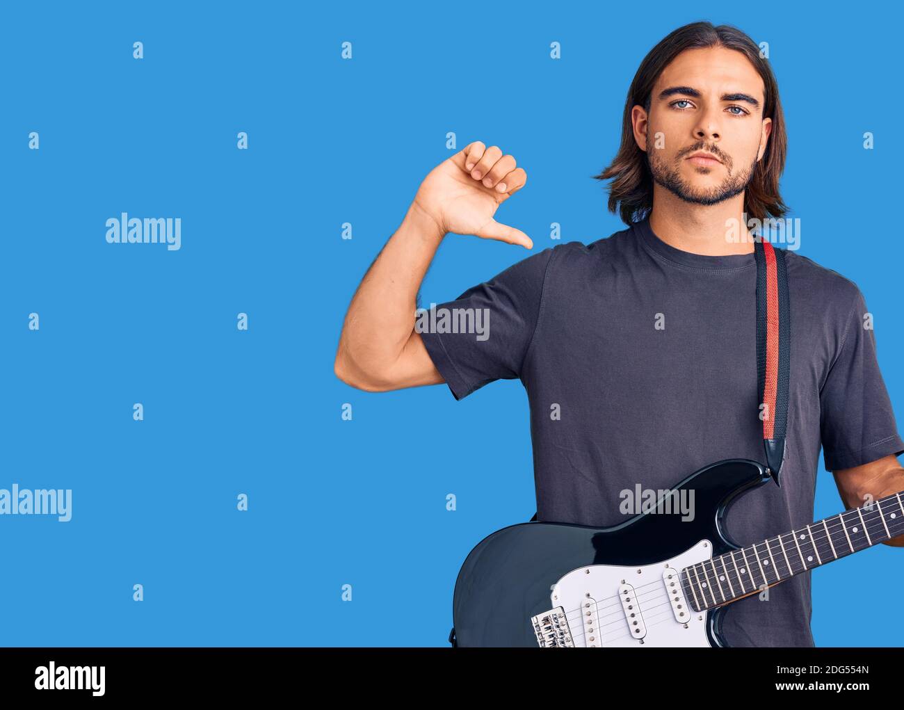 Young handsome man playing electric guitar with angry face, negative ...