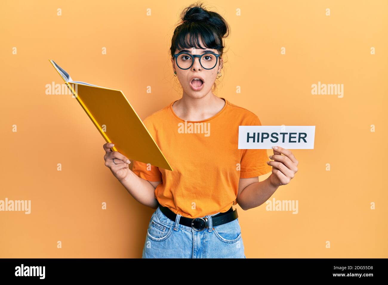 Young hispanic girl reading book and holding paper with hipster message ...