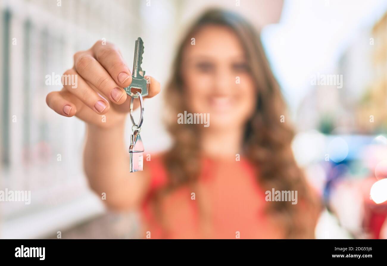 Young blonde girl smiling happy holding key of new house standing at ...