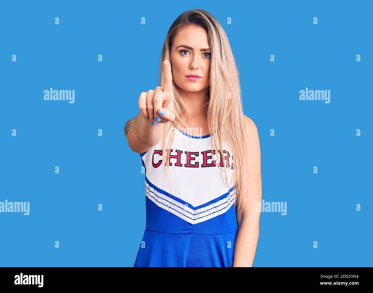 Young beautiful blonde woman wearing cheerleader uniform pointing with ...