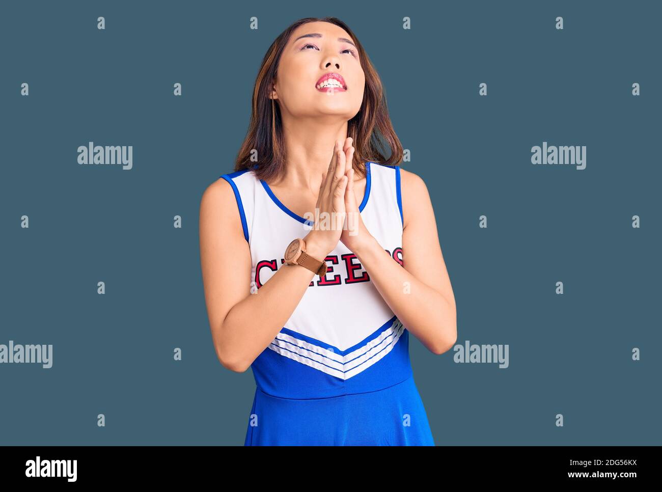 Young beautiful chinese girl wearing cheerleader uniform begging and ...