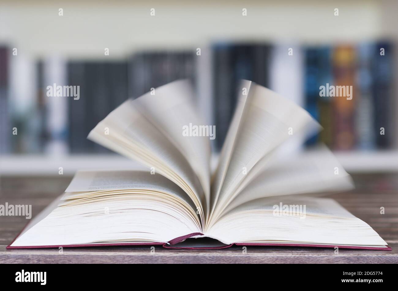 Opened book in front of bookcase with flying pages and motion blur with ...