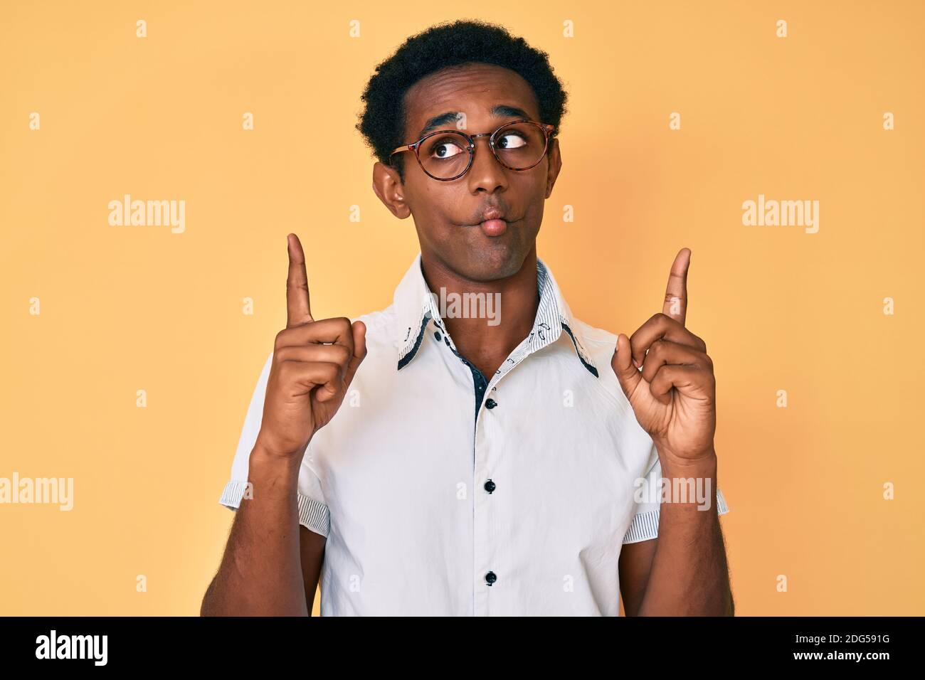 African handsome man pointing up with fingers making fish face with ...