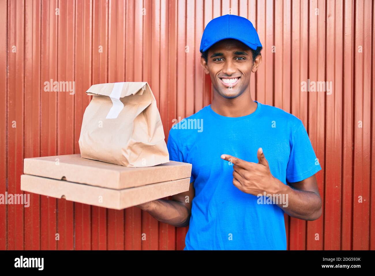 African delivery man wearing courier uniform outdoors holding take away ...