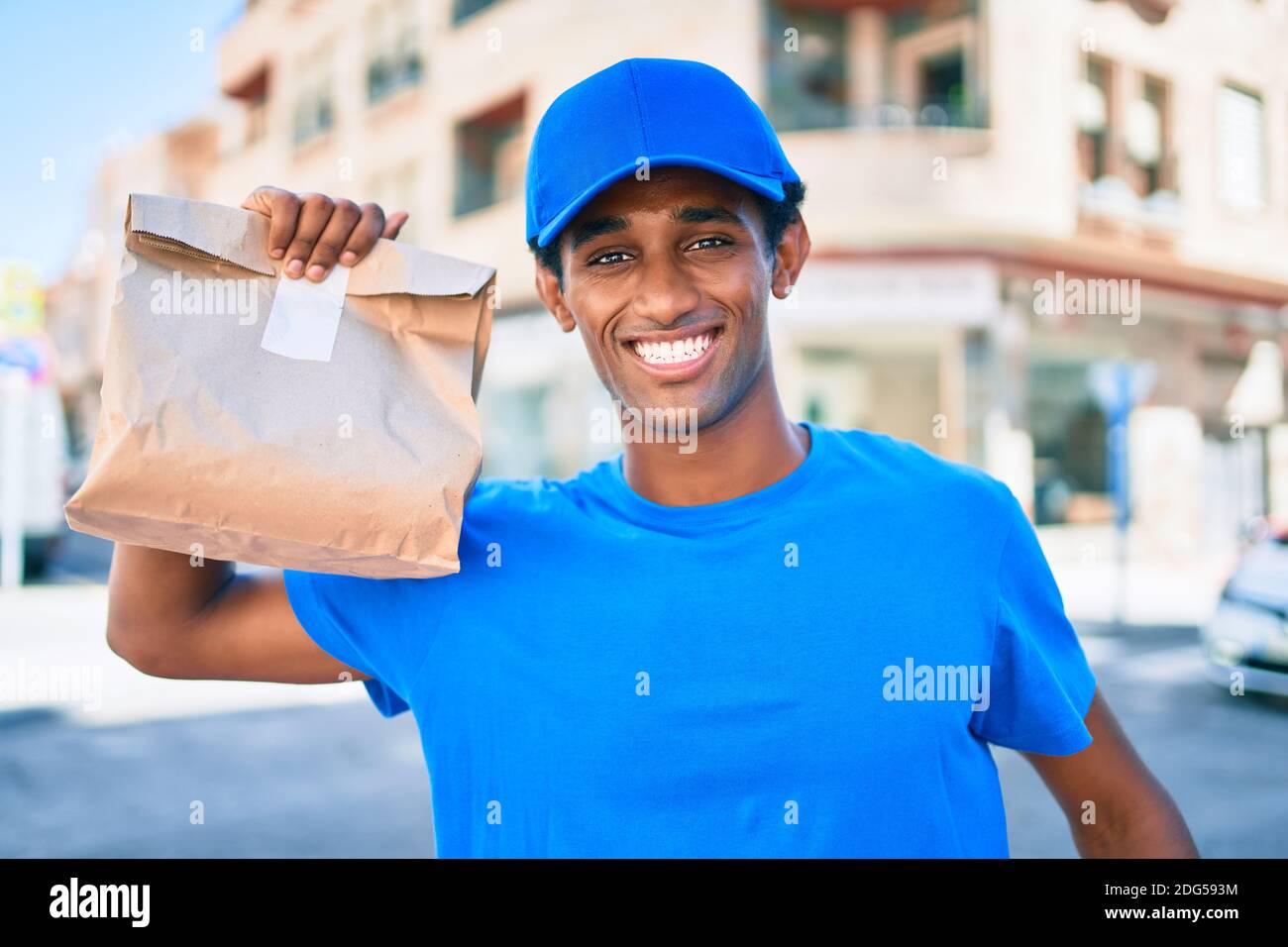 African delivery man wearing courier uniform outdoors holding take away ...