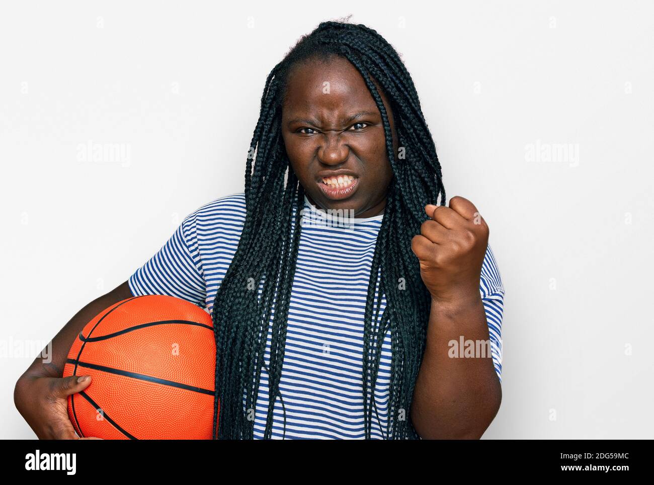 Young black woman with braids holding basketball ball annoyed and ...