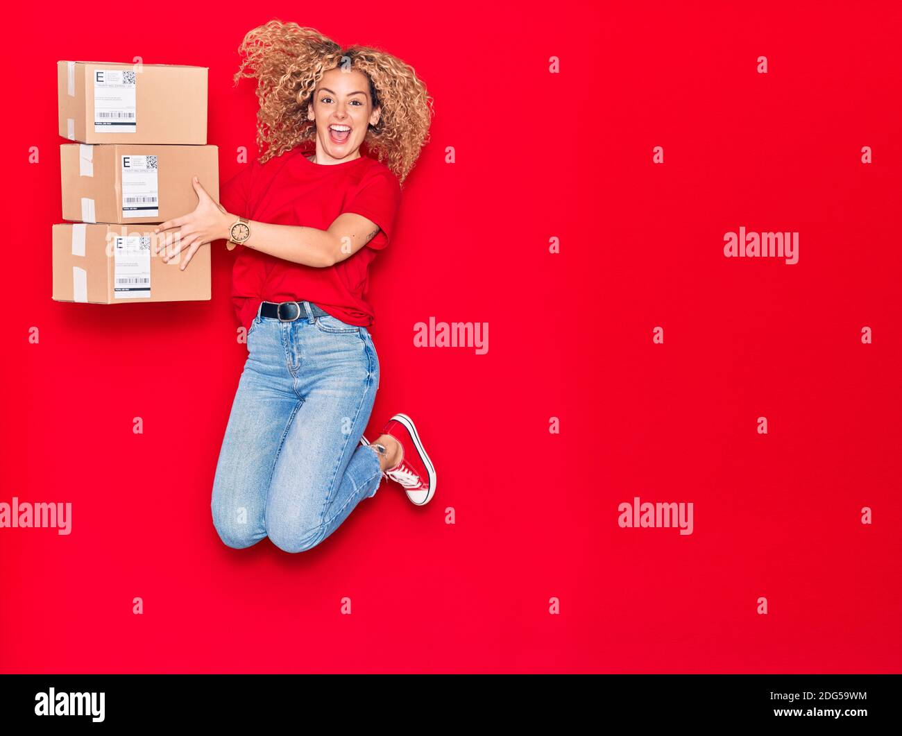 Young beautiful curly deliverywoman holding package smiling happy ...