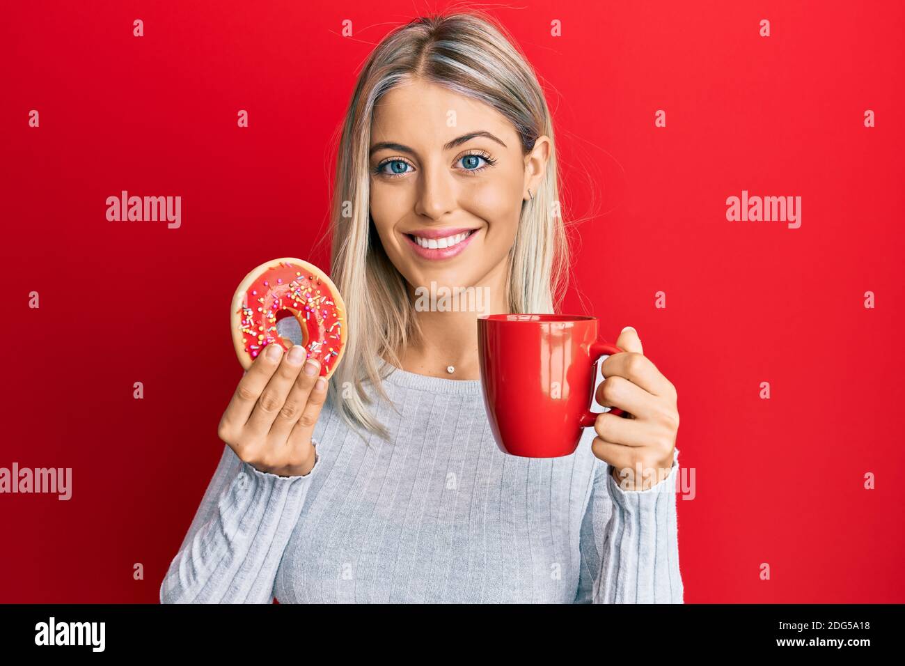 Beautiful blonde woman eating doughnut and drinking coffee smiling with ...