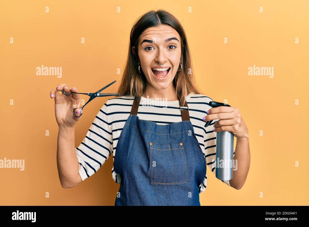 Young hispanic woman wearing hairdresser apron and holding scissors celebrating crazy and amazed ...